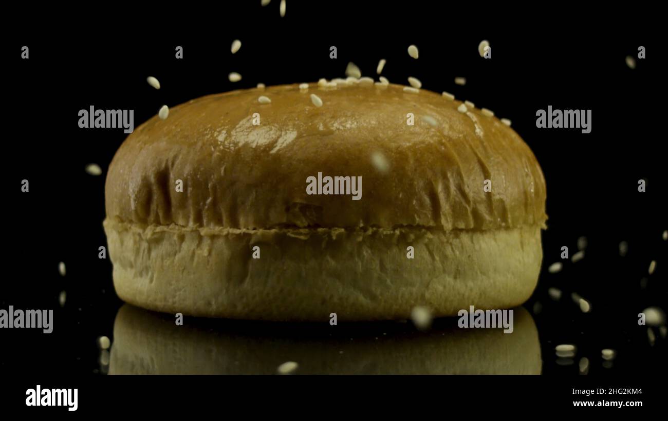 Close up of sesame seeds falling down on white burger bun isolated on ...