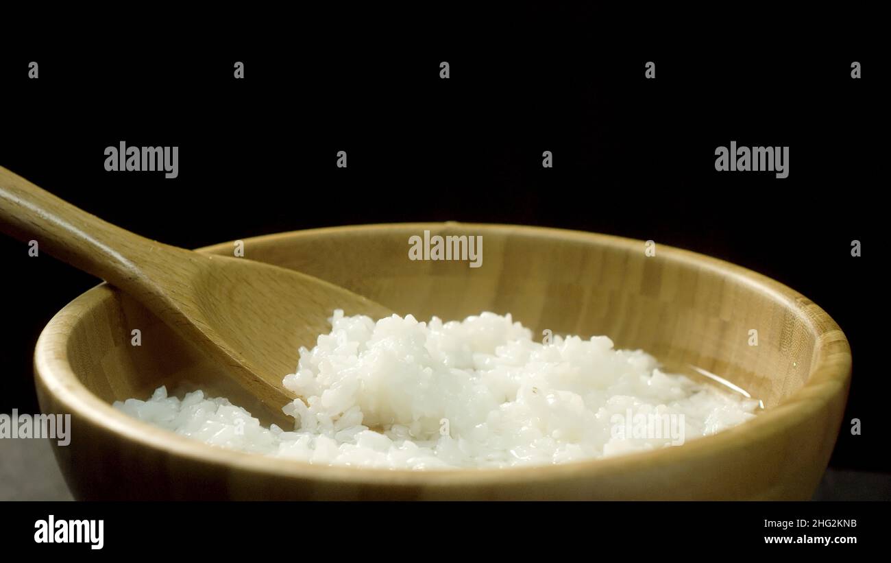 Close up for steamed rice in a wooden bowl with wooden stirring spoon ...
