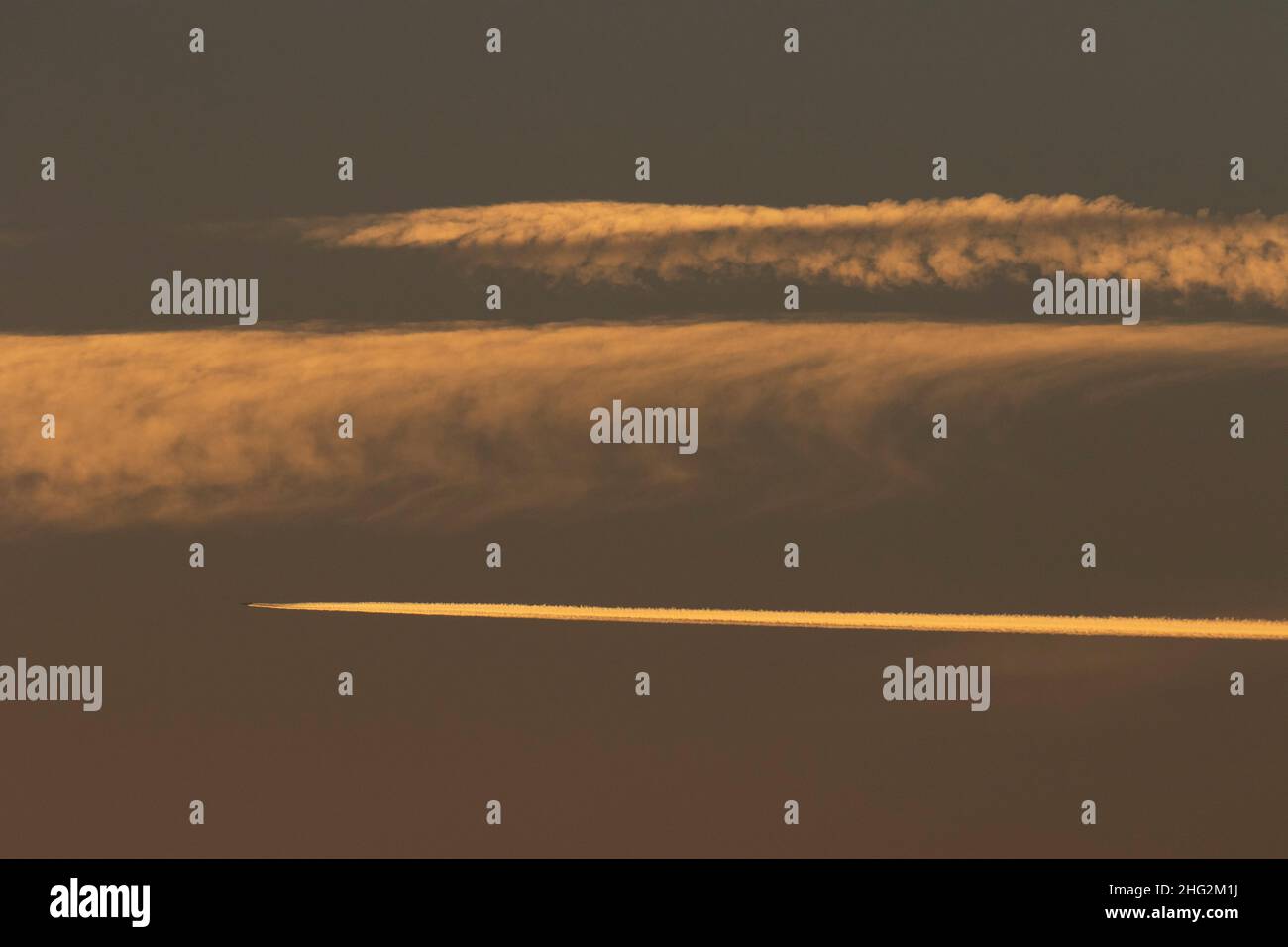 A commercial jet produces a colorful contrail below a layer of previous ...