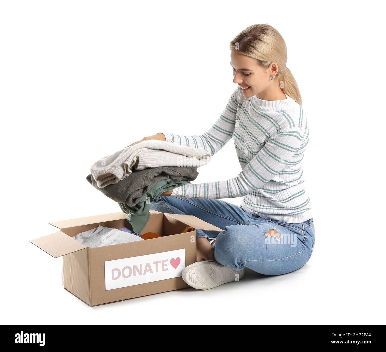 Young woman putting donation clothes in box on white background Stock ...