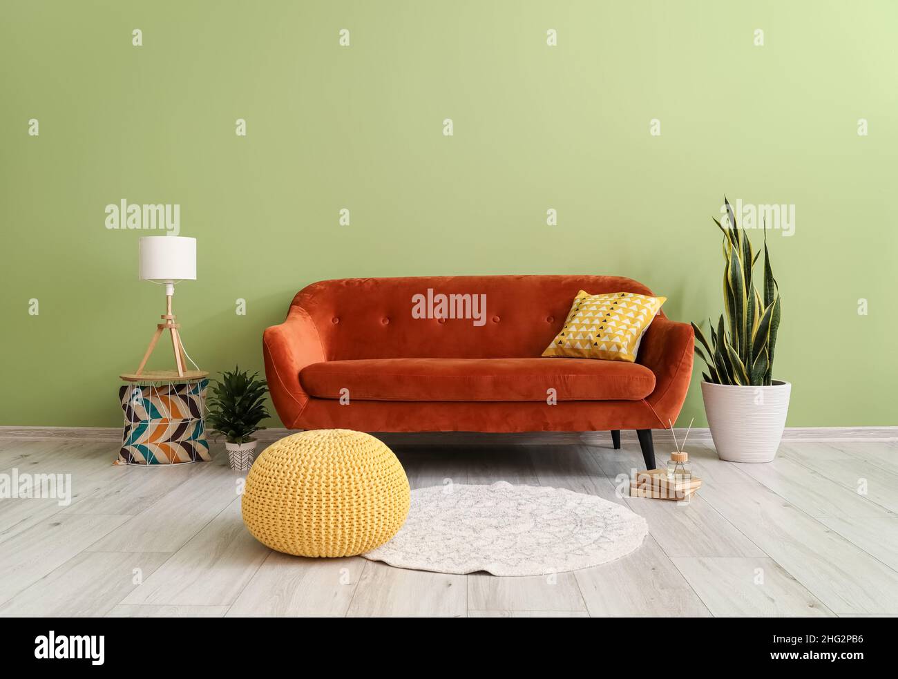 Sofa, pouf and houseplant near color wall Stock Photo - Alamy