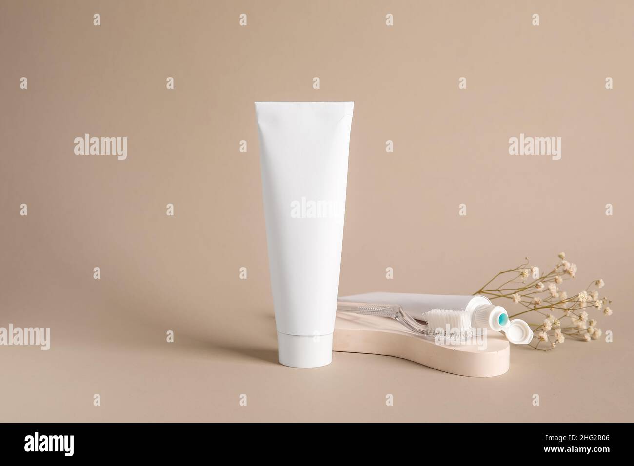 Composition with toothpaste tubes, toothbrush and flowers on beige ...