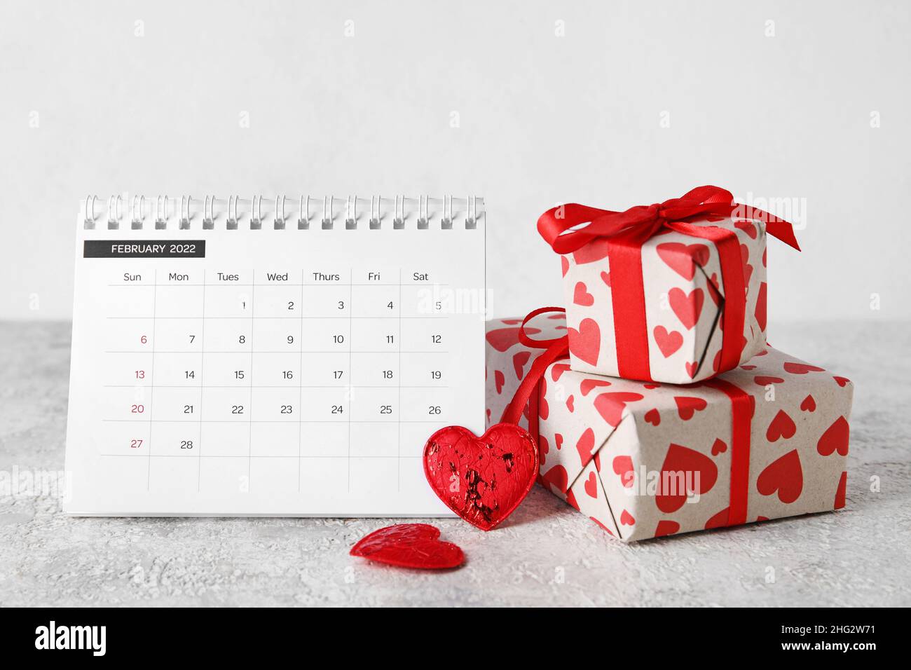 Calendar with gifts and hearts on table against white background ...