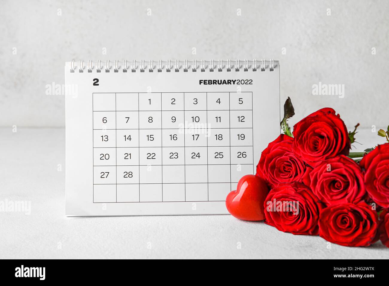 Calendar with red roses on table against light background. Valentine's ...