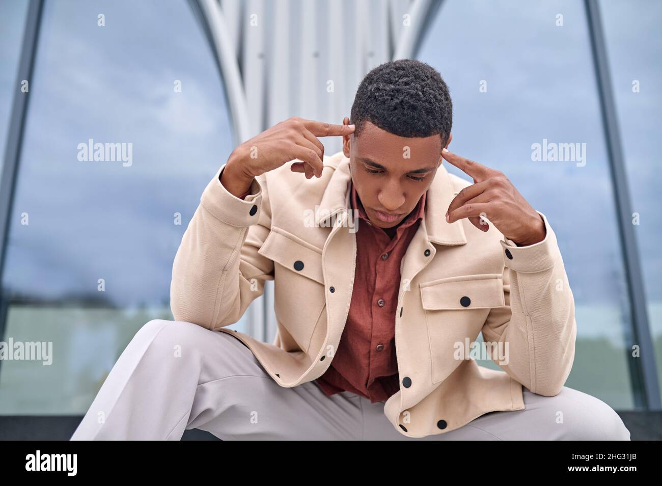 Man touching fingers to head sitting thinking outdoors Stock Photo - Alamy
