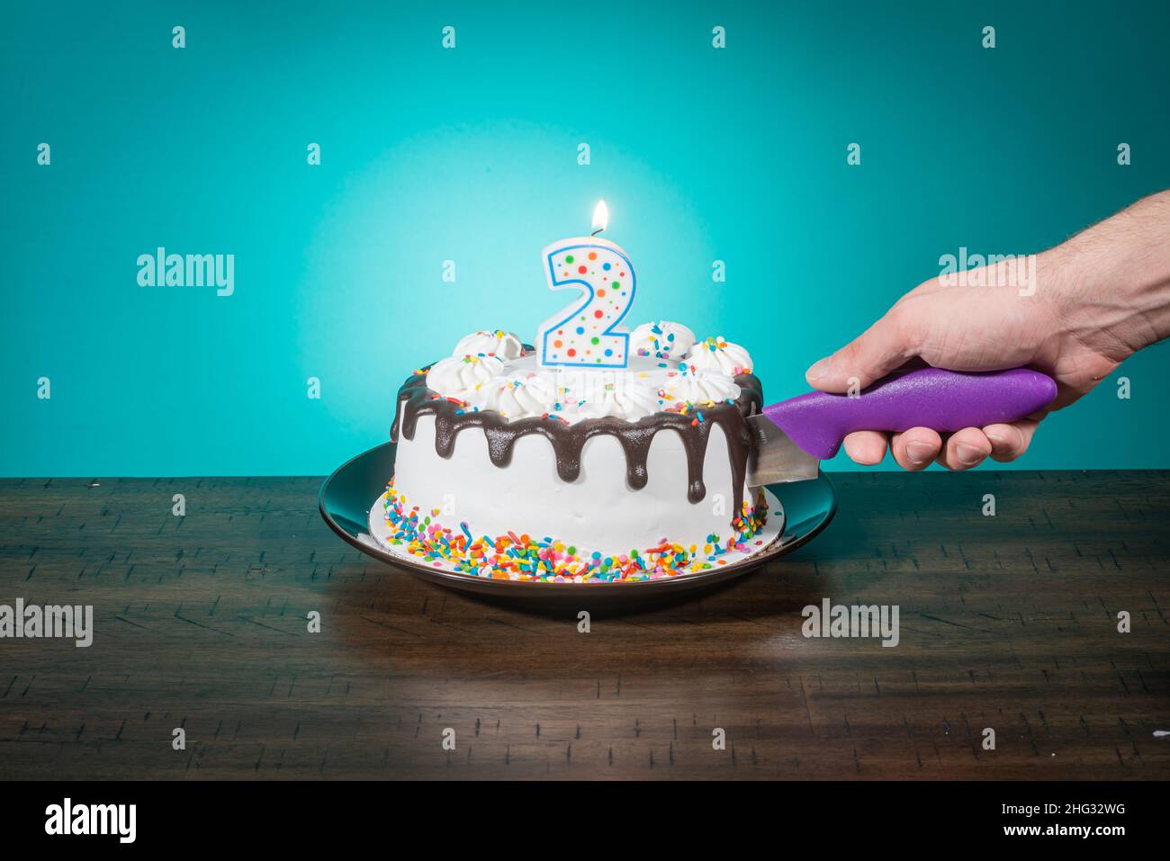 A birthday cake bears a candle in the shape of the number 2 while a ...