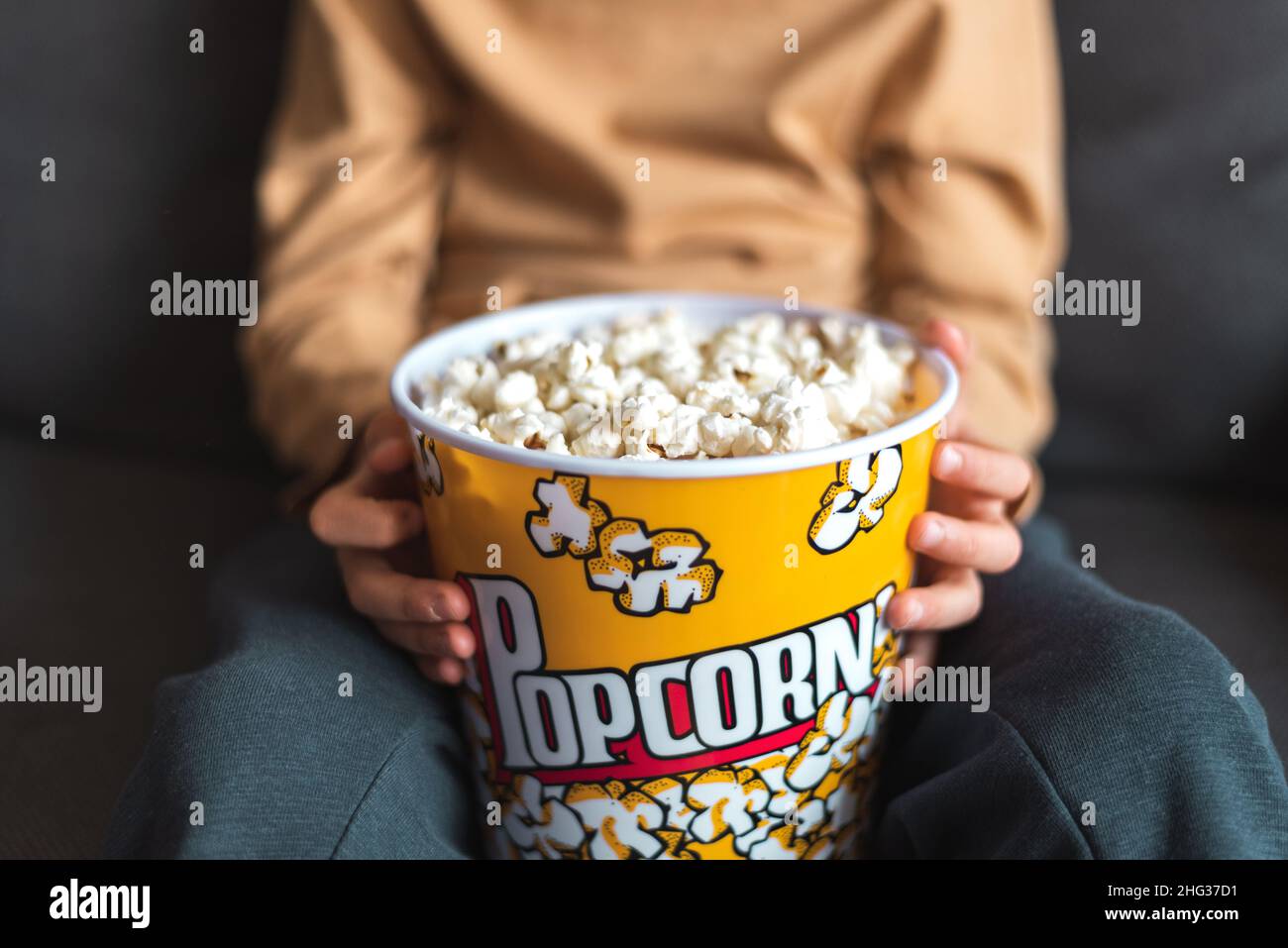 Crop anonymous child in casual clothes eating bucket of popcorn while ...