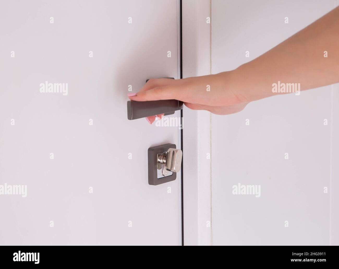 A woman's hand presses the handle of a modern white door to a room ...