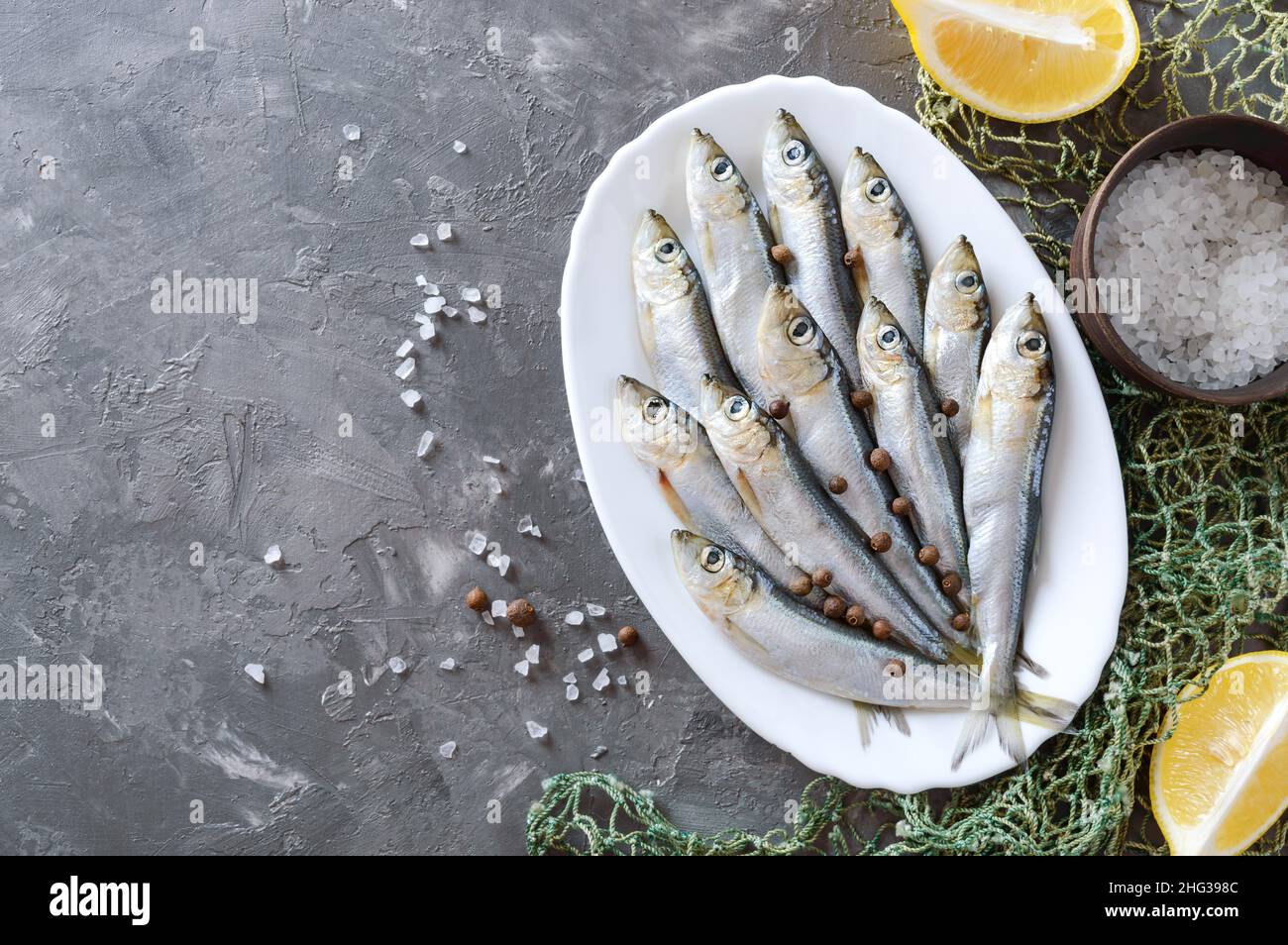 Freshly caught sea small fish on a plate on a gray concrete background ...