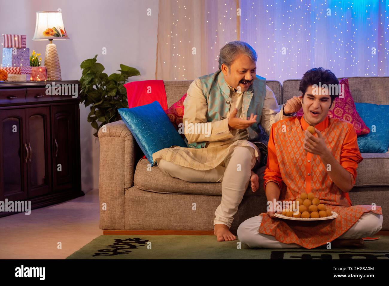 Father pulling ear of his son while eating ladoo on Diwali Stock Photo ...