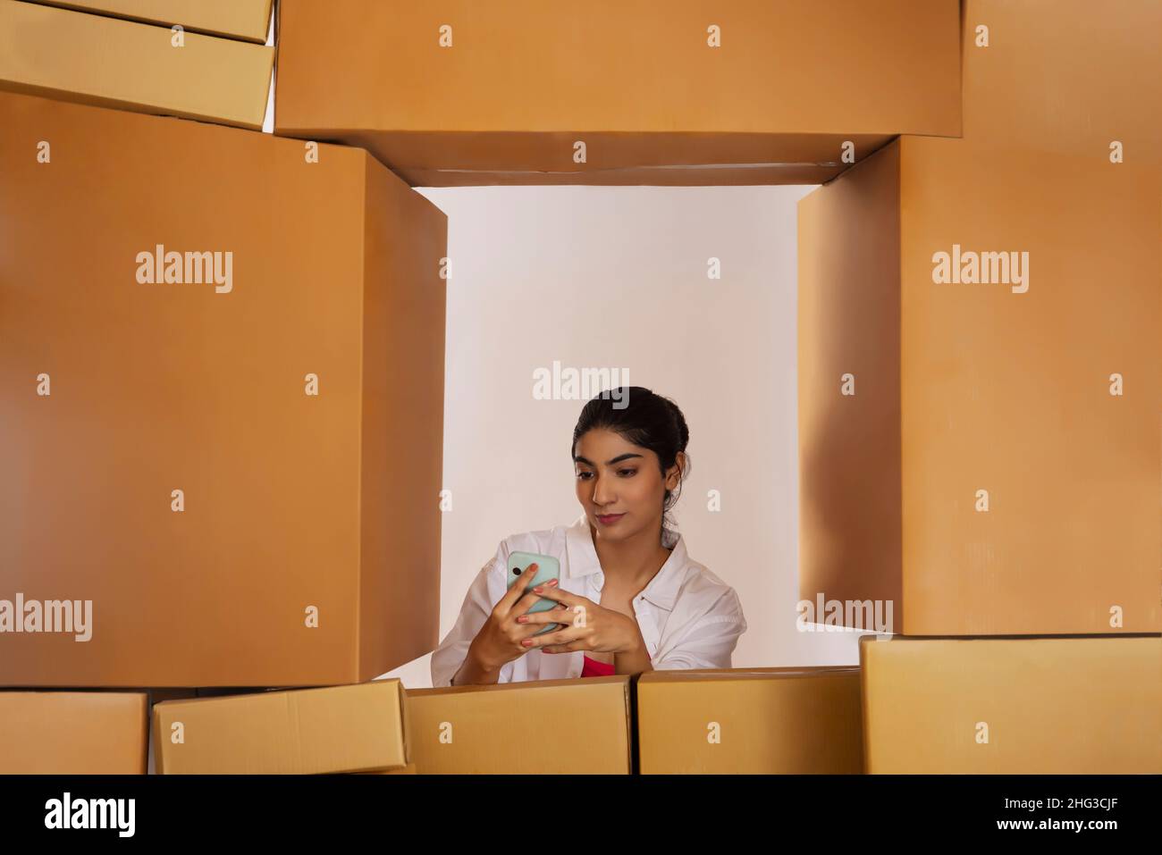 Adult girl watching Smartphone behind stacking of cardboard boxes Stock ...