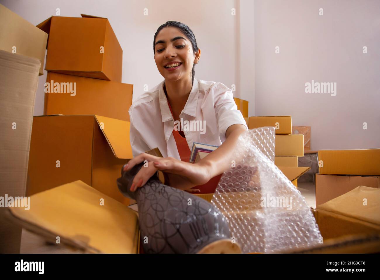 Adult girl packing flower vase with bubble wrap into cardboard box ...