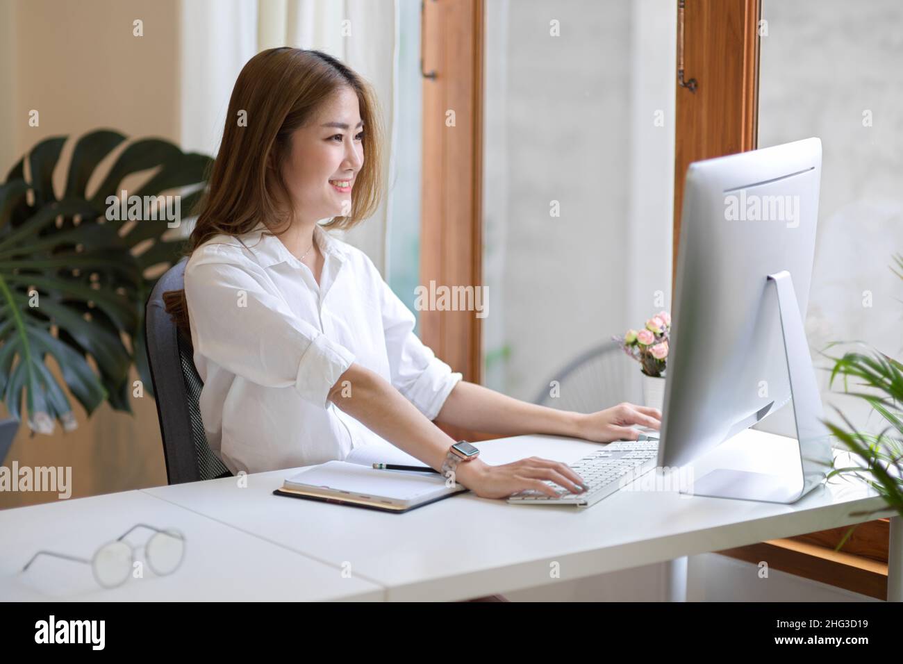 Happy Asian young businesswoman using desktop computer in her modern ...