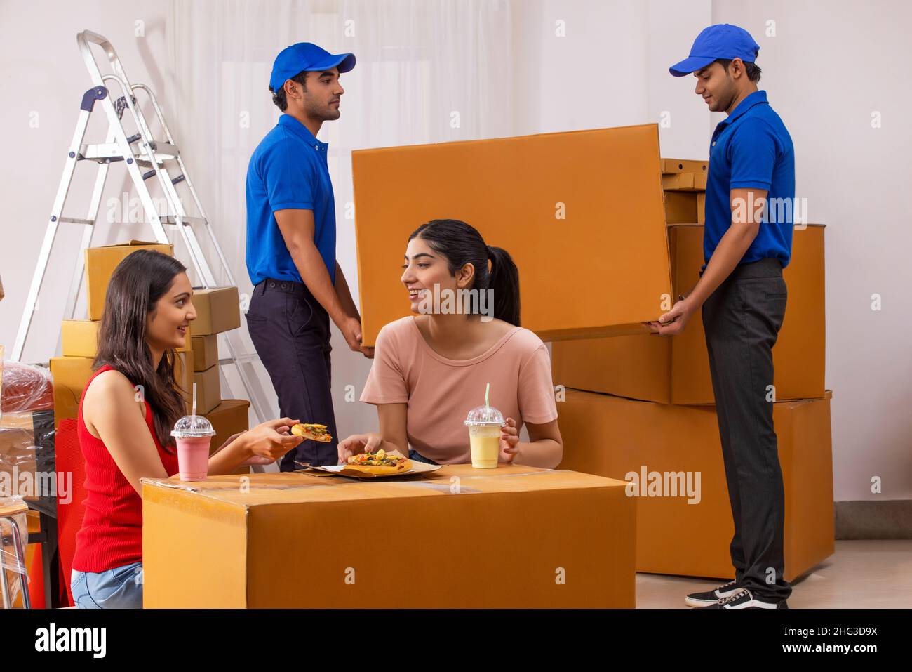 Adult girls eating pizza while the delivery boys moving cardboard boxes ...
