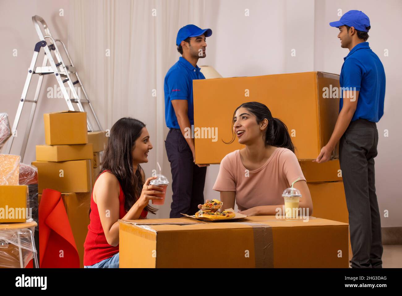 Adult girls eating pizza while the delivery boys moving cardboard boxes ...