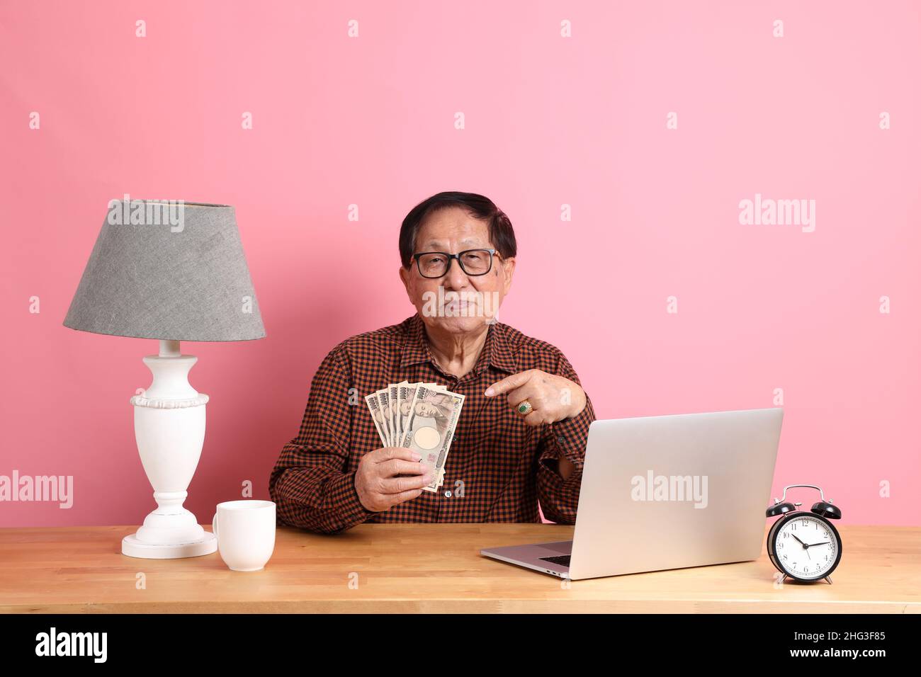 The senior Asian man sitting at working desk with laptop on the pink ...