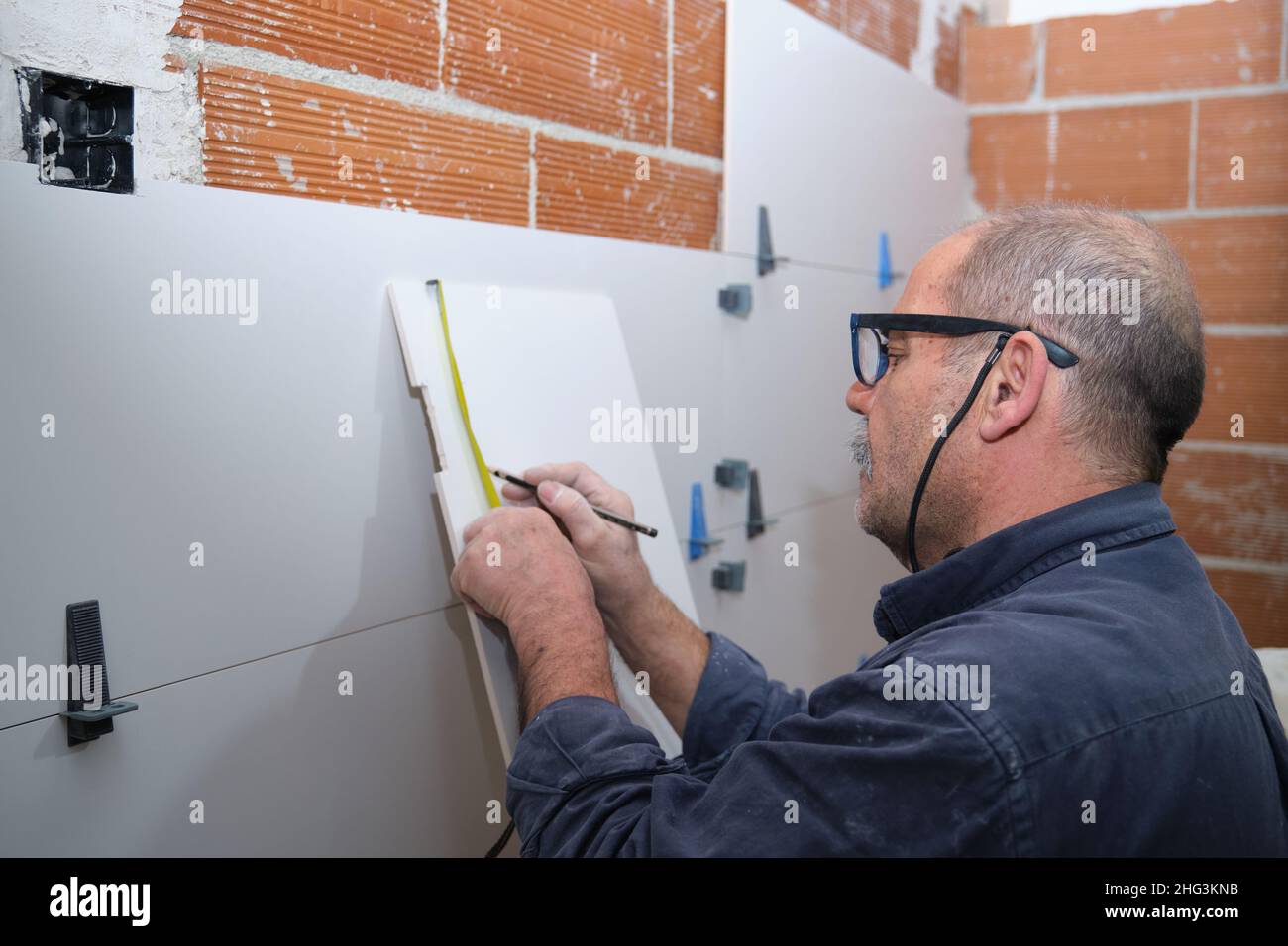 Professional tiler measuring a white ceramic tile to fit the wall Stock ...