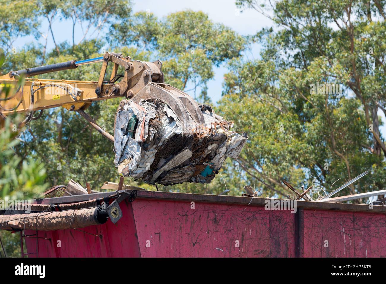 An excavator claw holds a large block of crushed used steel over a ...