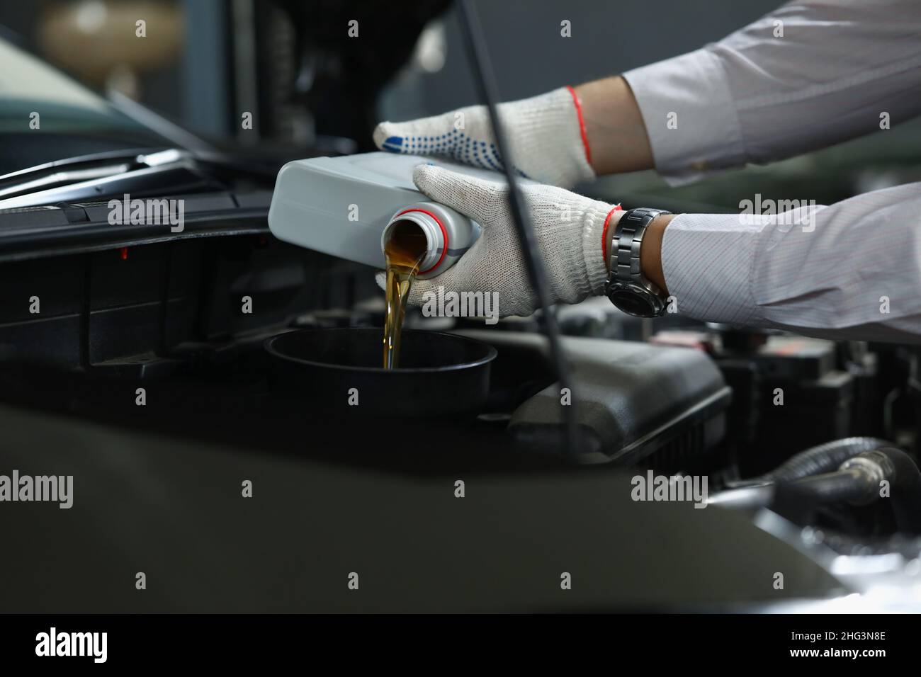Worker refueling and pouring new oil into engine motor of automobile ...
