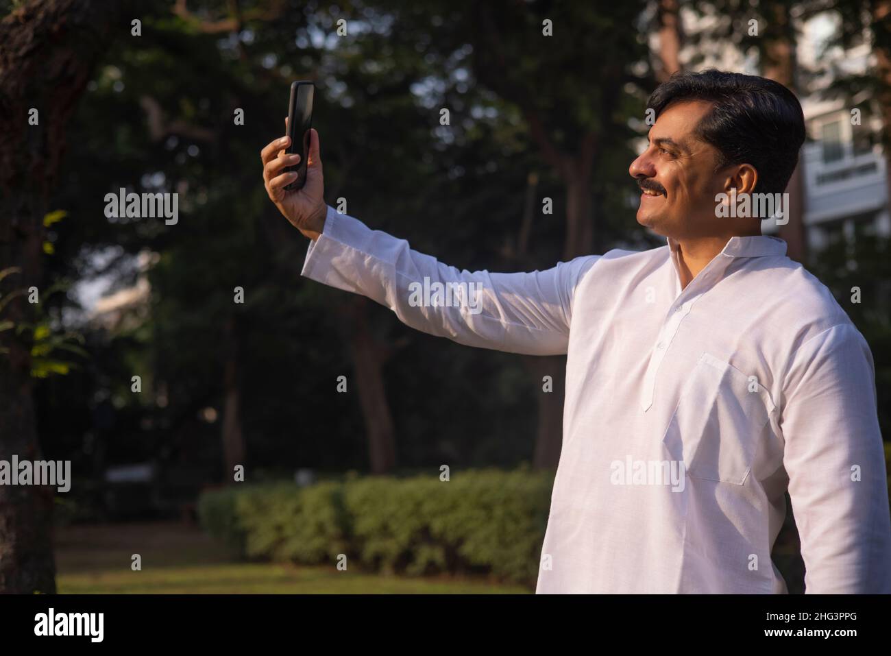 Man in white kurta taking selfie while standing in park in the morning ...