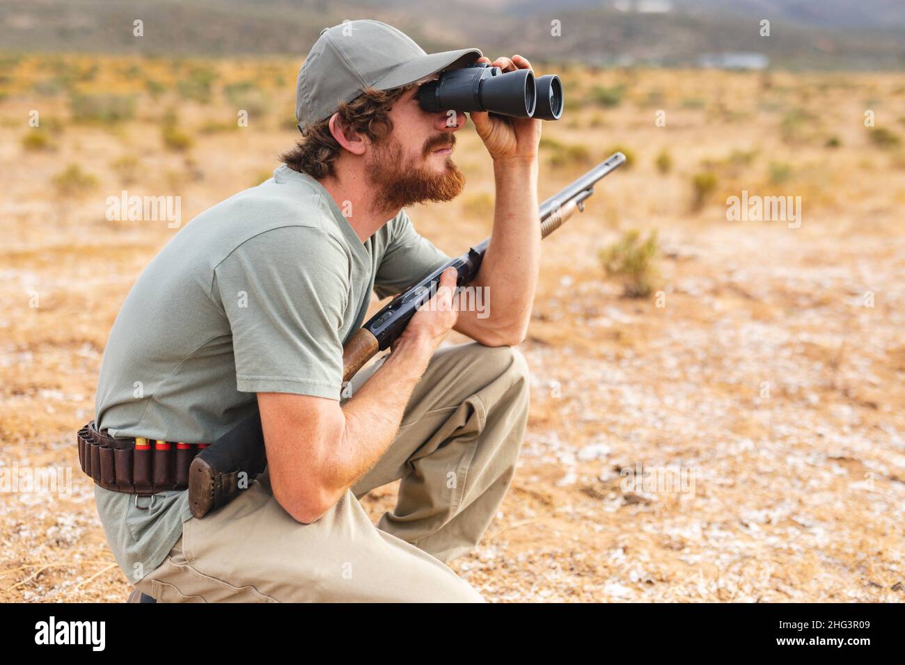Side view of young caucasian male hunter crouching with rifle while ...