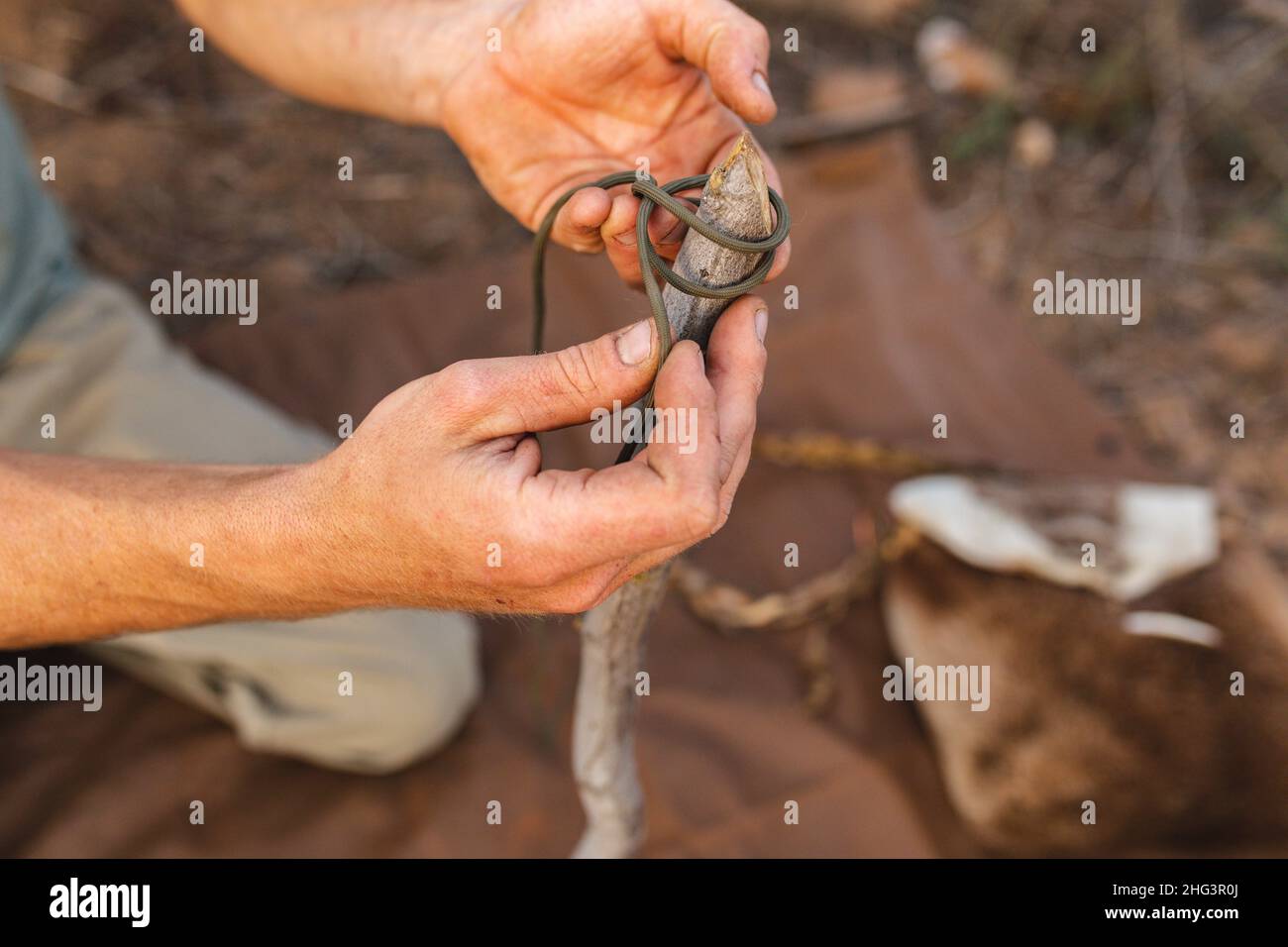 Cropped hands of young male caucasian survivalist tying string on stick ...