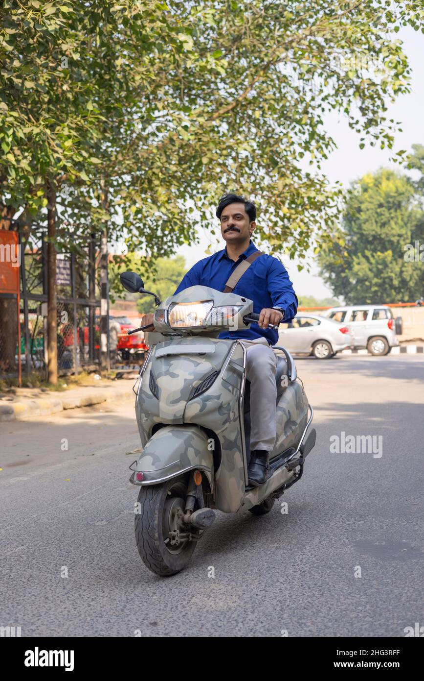 Common man riding a scooty on city street Stock Photo - Alamy