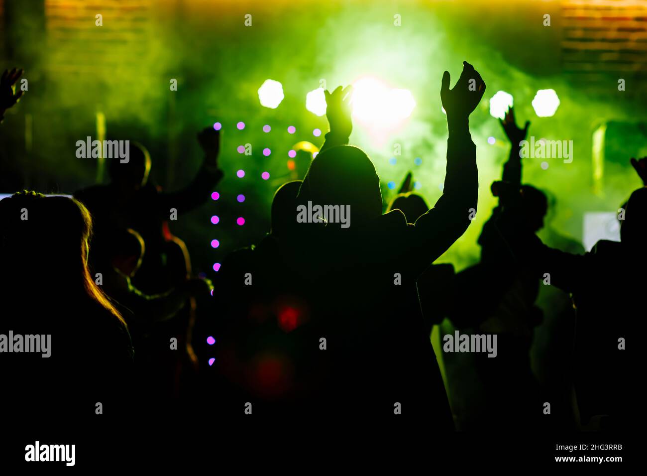 cheering crowd in front of bright yellow green stage lights. Silhouette ...