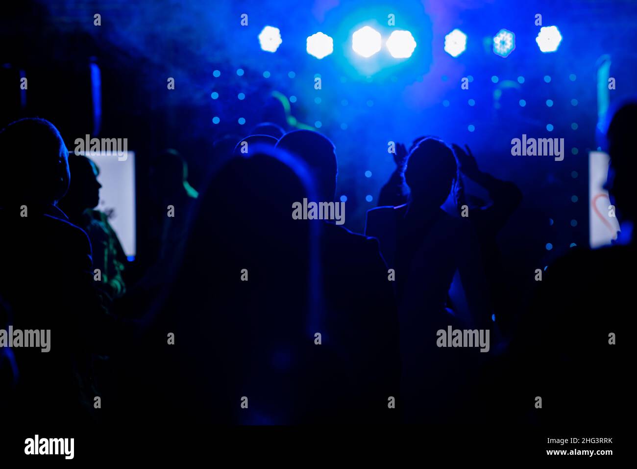 cheering crowd in front of bright blue stage lights. Silhouette image ...