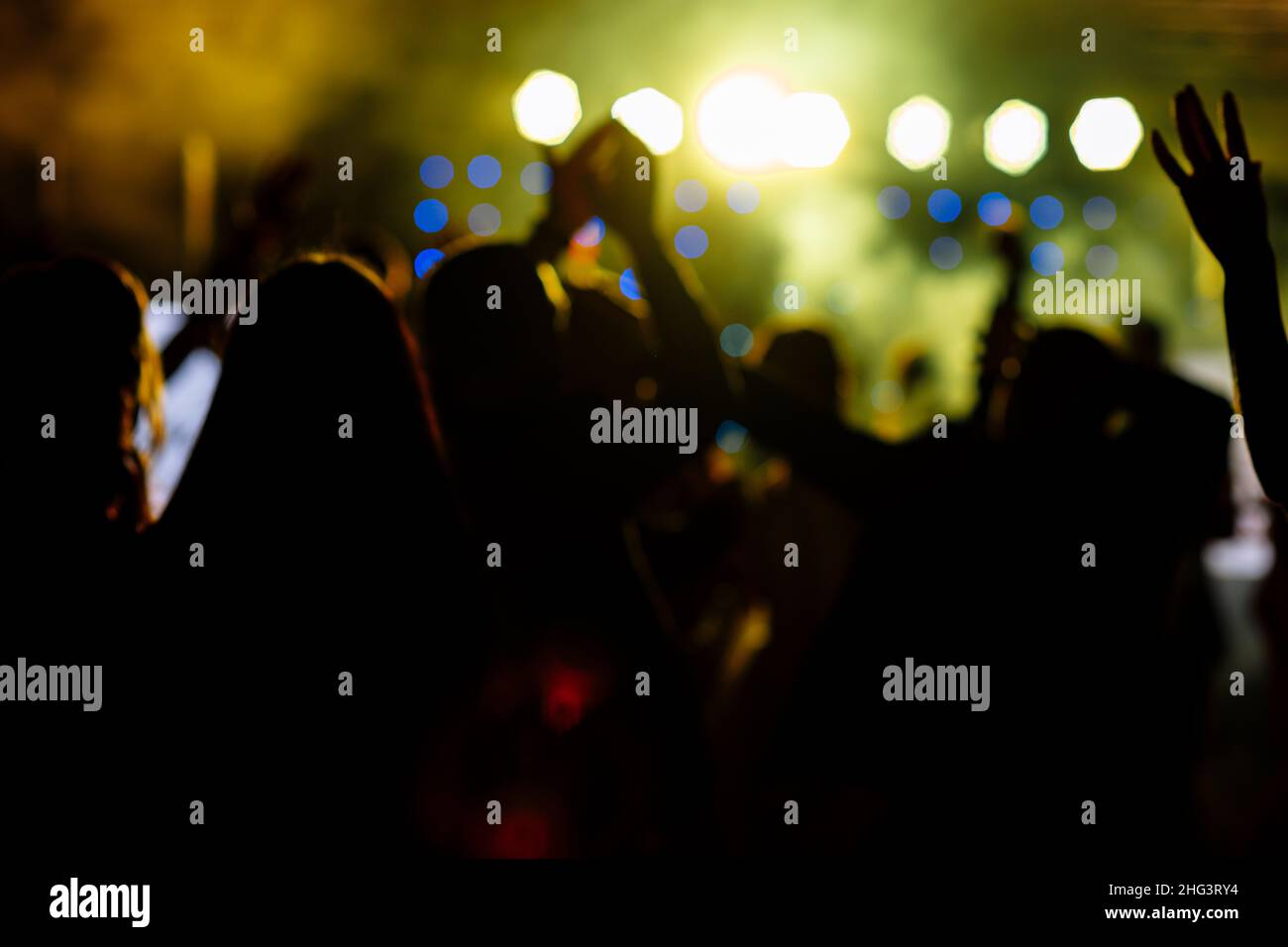 cheering crowd in front of bright yellow stage lights. Silhouette image ...