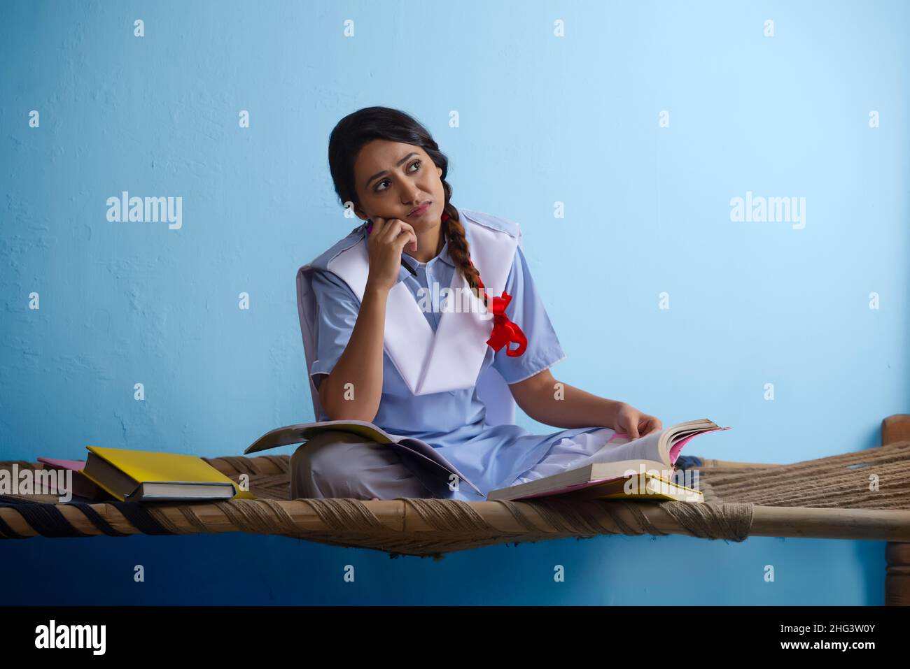 A girl in school uniform thinking while studying on cot at home Stock ...