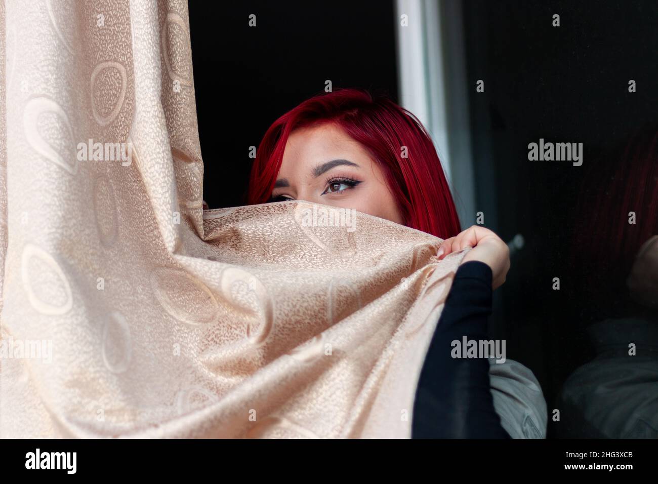 Thoughtful teenage girl behind the curtain, looking outside. Young girl ...