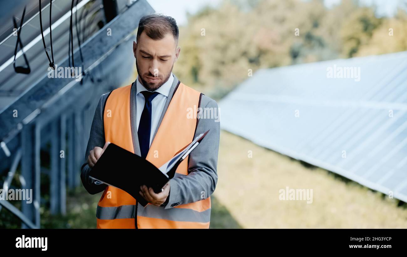 businessman in safety vest holding folder with documents near solar ...