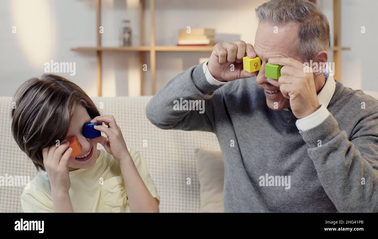 middle aged grandfather and funny grandson holding building blocks near ...