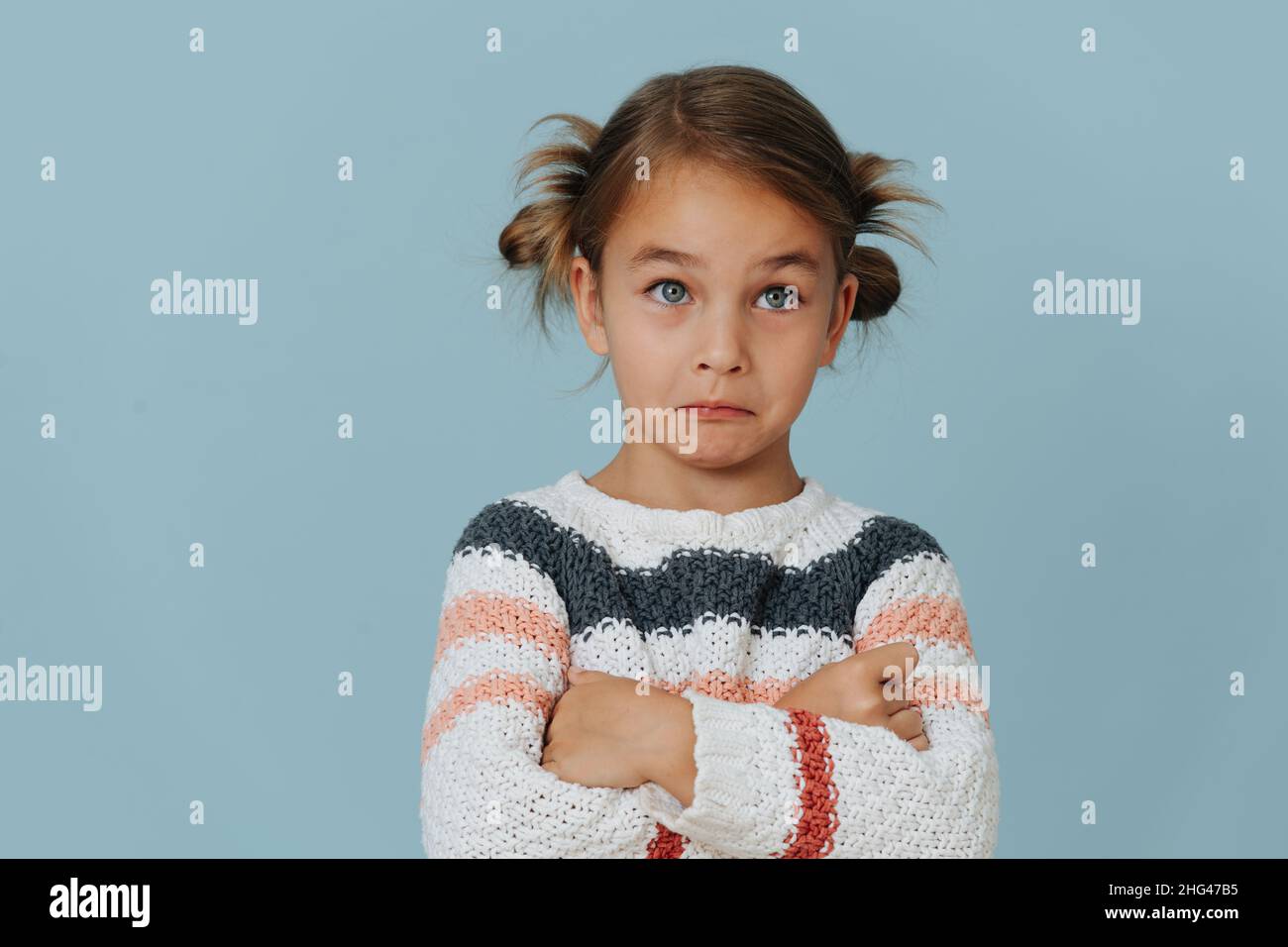 Pouting little girl in striped sweater standing with hands crossed ...