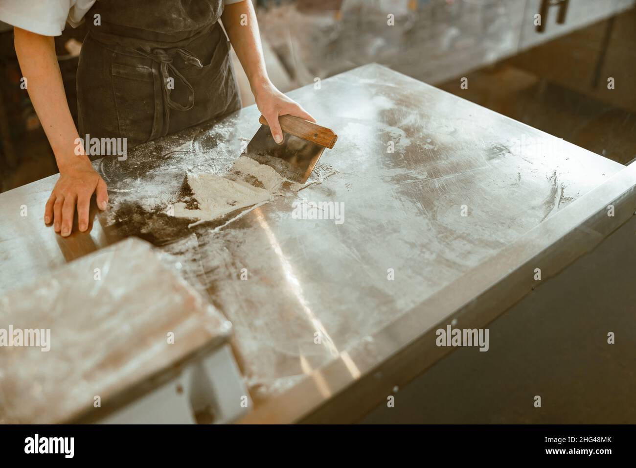 Female worker stands at table with pile of white flour and cutting tool ...