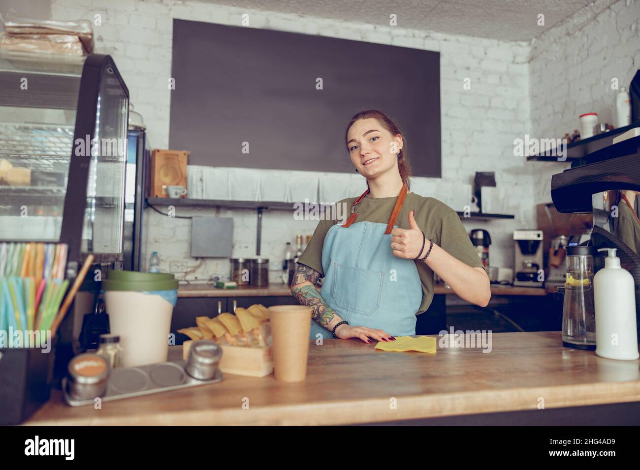 Cheerful woman standing behind counter and giving thumbs up Stock Photo ...