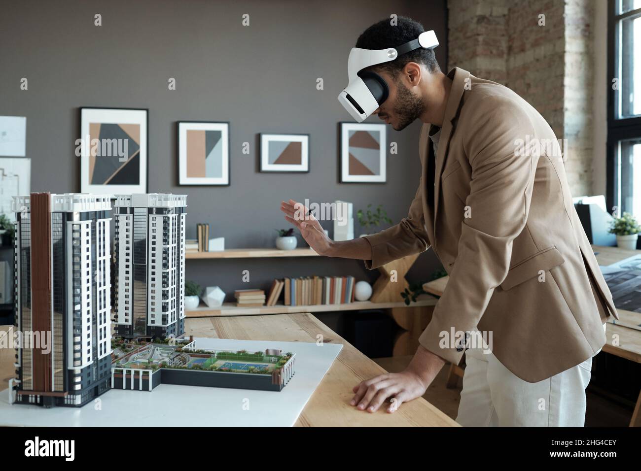 Young elegant architect in vr headset standing by table with house ...