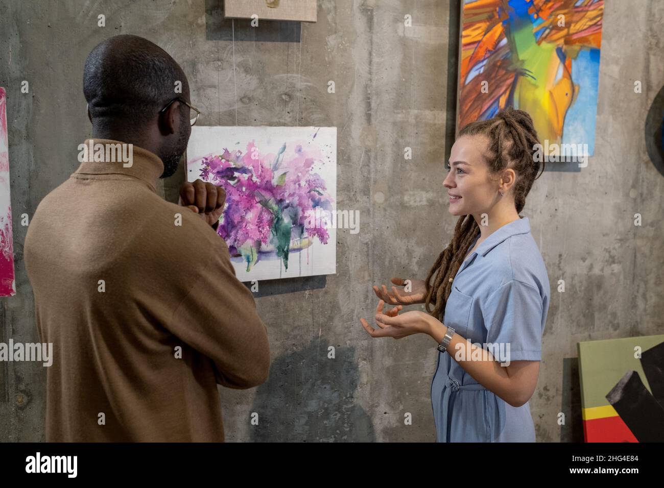 Young female guide describing one of paintings on walls to African man ...