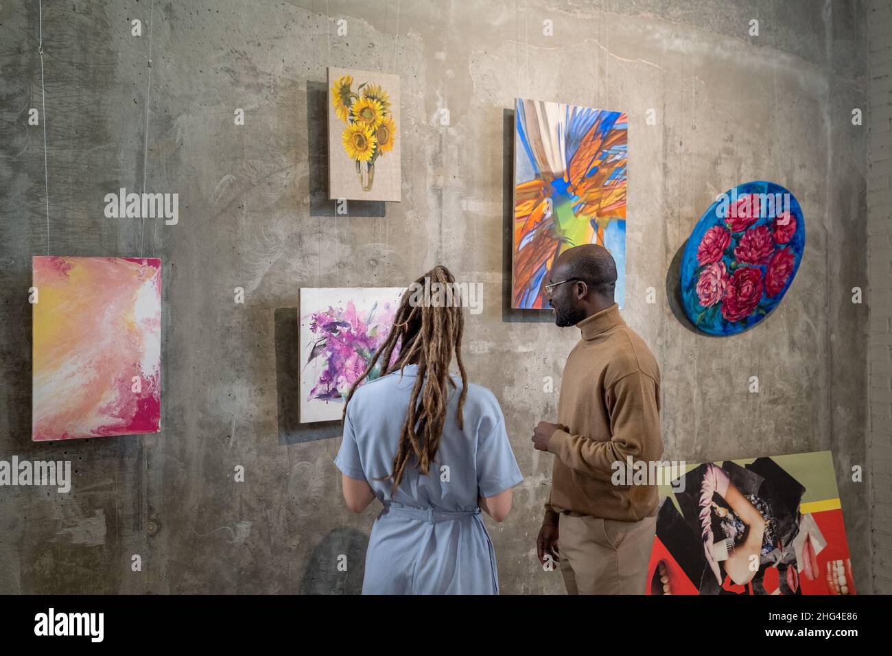 Young intercultural man and woman discussing one of paintings on wall ...