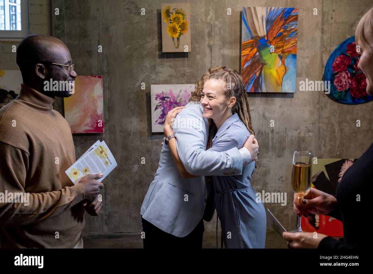 Happy young female embracing modern artist while standing against wall ...