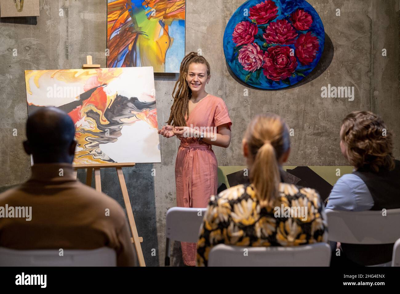 Happy young female auctioneer presenting abstract painting to audience ...