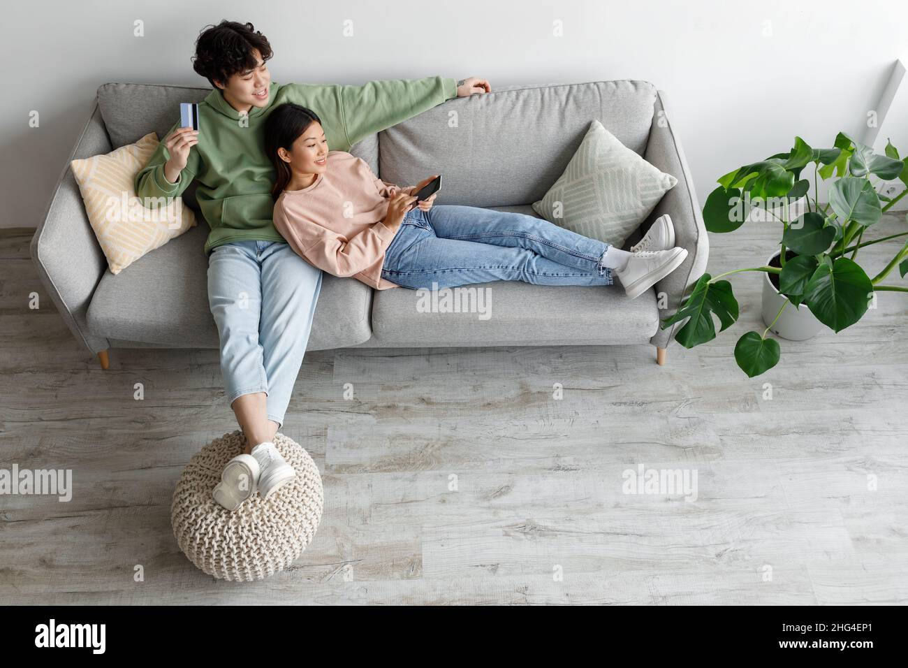 Happy Asian couple sitting together on couch at home, holding ...
