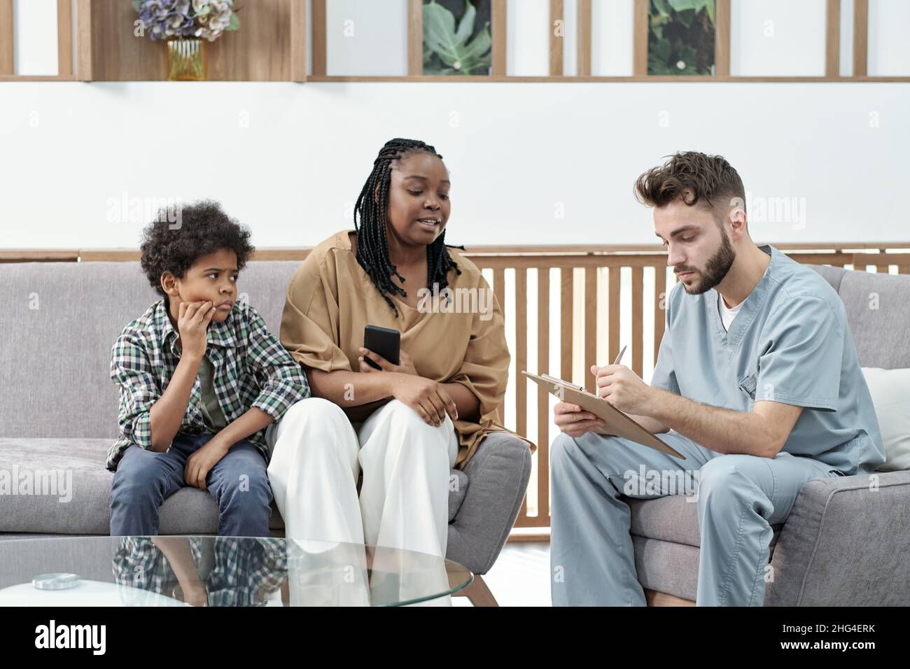 African Woman And Her Son With Toothache Looking At Dentist With Clipboard Pointing At Document