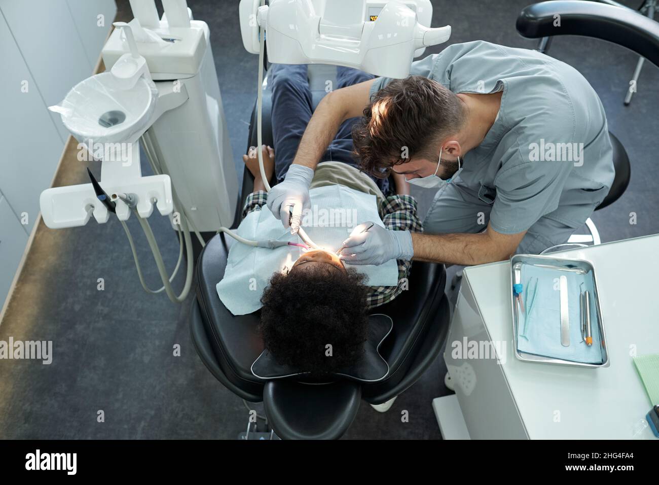 Male stomatologist in uniform bending over little African boy during ...