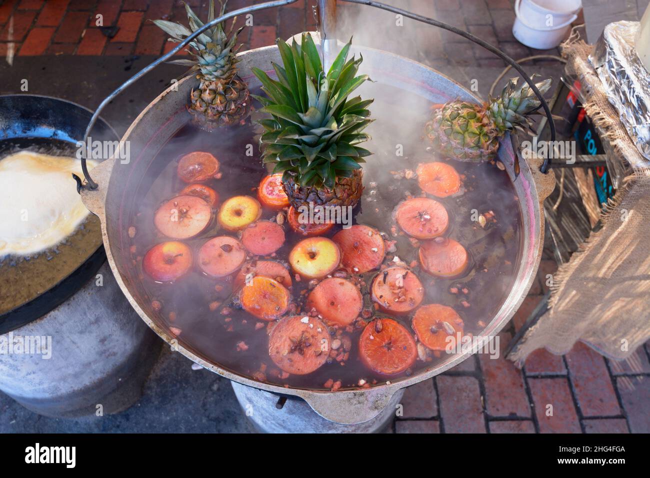 Preparing mulled wine at outdoor stall. Pineapples boiling in wine in ...