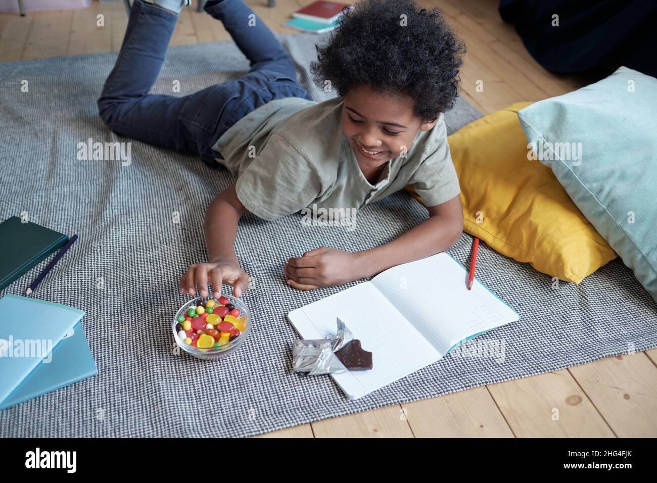Smiling cute boy taking candy out of glass bowl while relaxing on the ...