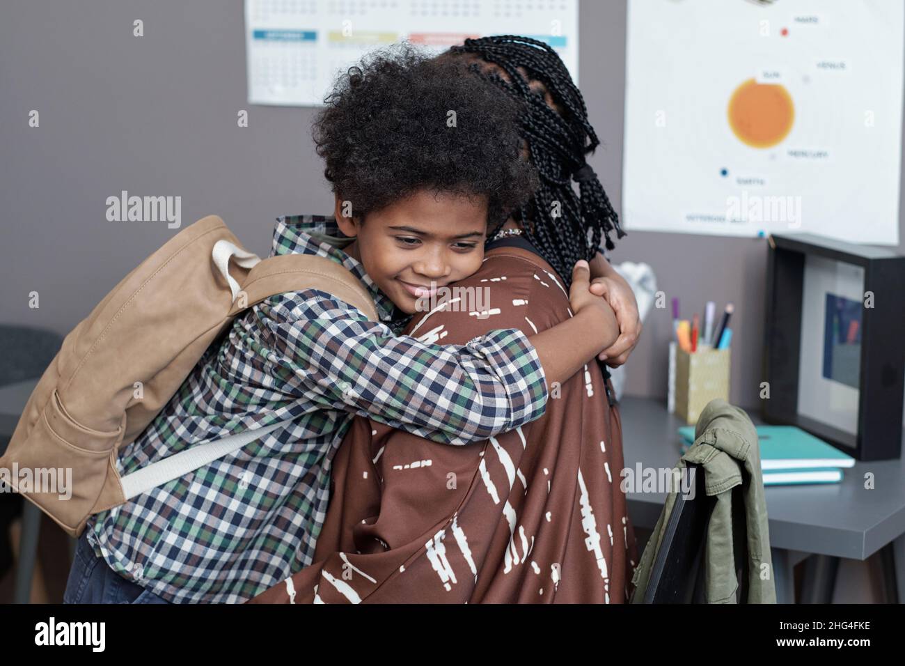 Happy affectionate schoolboy with backpack giving hug to his mother ...