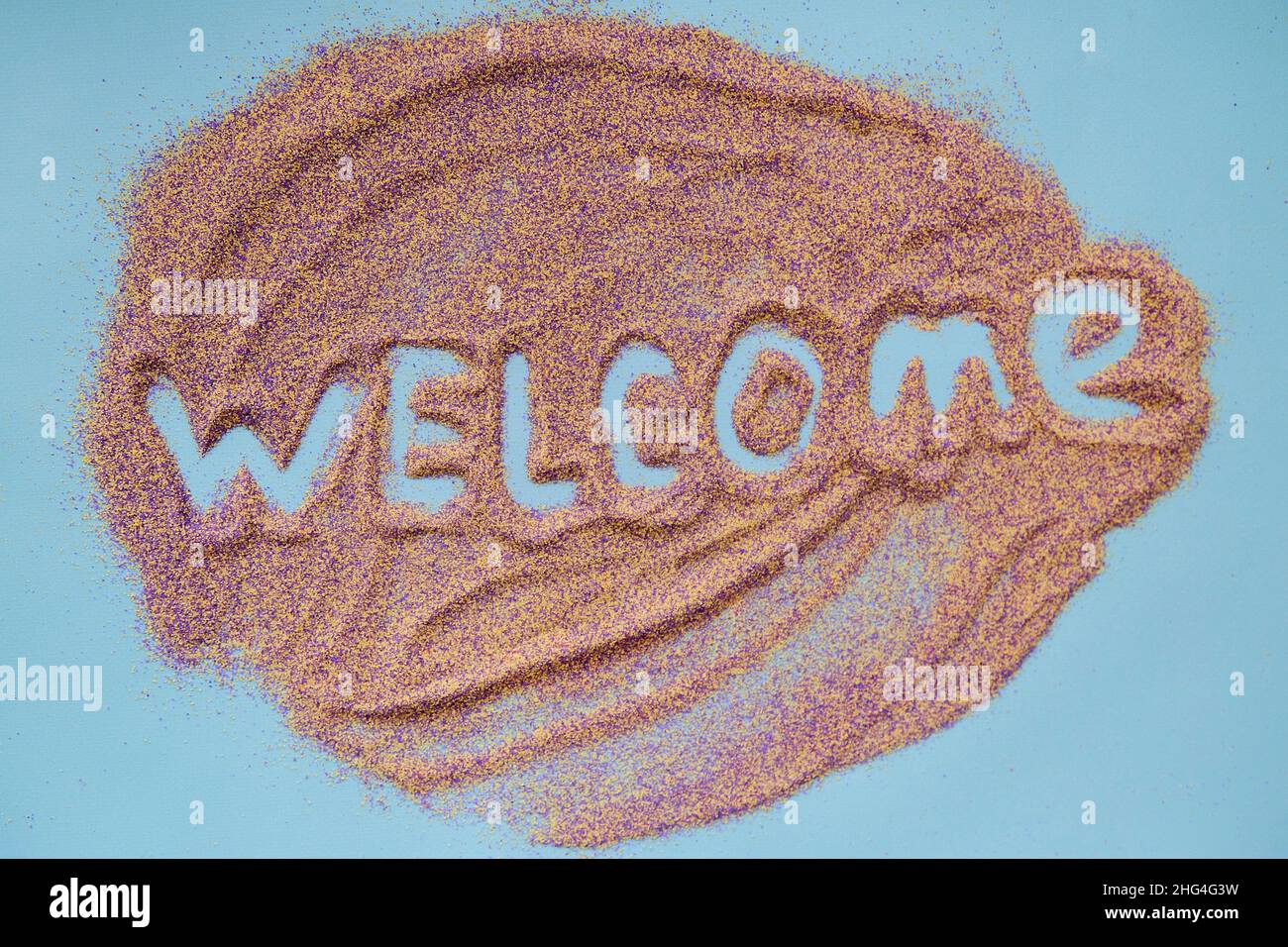 Welcome handwritten text on colorful sand in shape of leaf. Close up ...