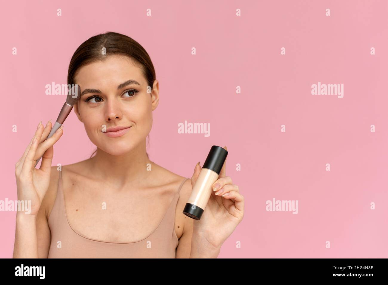 A beautiful smiling model applies foundation from a glass tube ...